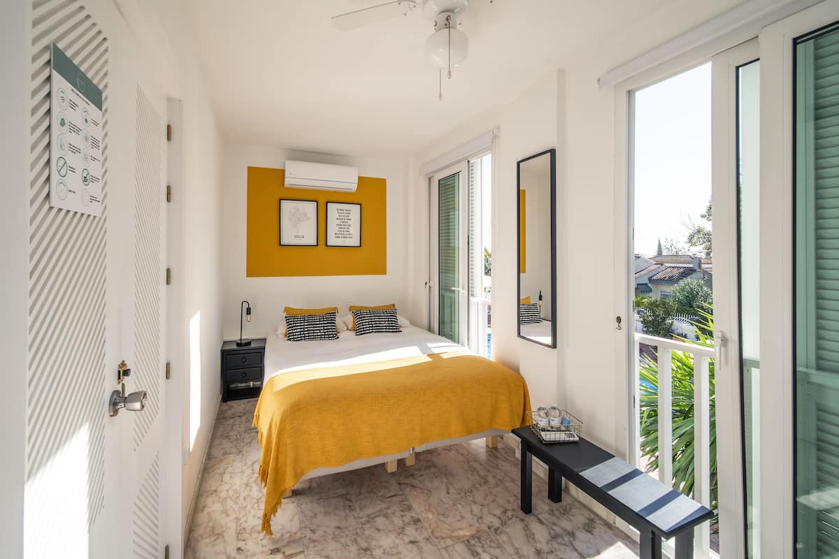 Quarto com cama, mesa de cabeceira, janela e porta.
