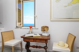 Quarto com escrivaninha, duas cadeiras, janela com vista, vaso e mapa na parede.