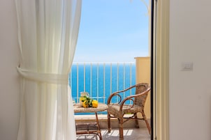 Varanda com móveis de vime, uma mesa com limões e vista para o mar.