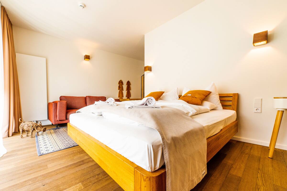 Quarto moderno com cama de madeira, sofá vermelho e tapete pequeno.