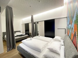 Quarto de hotel moderno com uma cama grande, um espaço de estar separado e uma pintura abstrata colorida na parede.