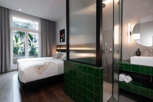 Quarto de hotel moderno com uma cama grande, área de chuveiro e parede com azulejos verdes.