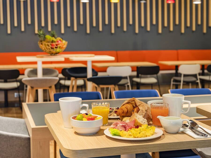 Mesa posta para dois com croissant, tigela de frutas, suco de laranja e ovos mexidos.