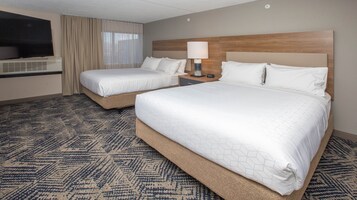 Quarto de hotel com duas camas, uma televisão, um abajur e um tapete estampado.