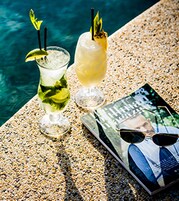 Duas bebidas com canudos e rodelas de limão sobre uma superfície texturizada perto de uma piscina.