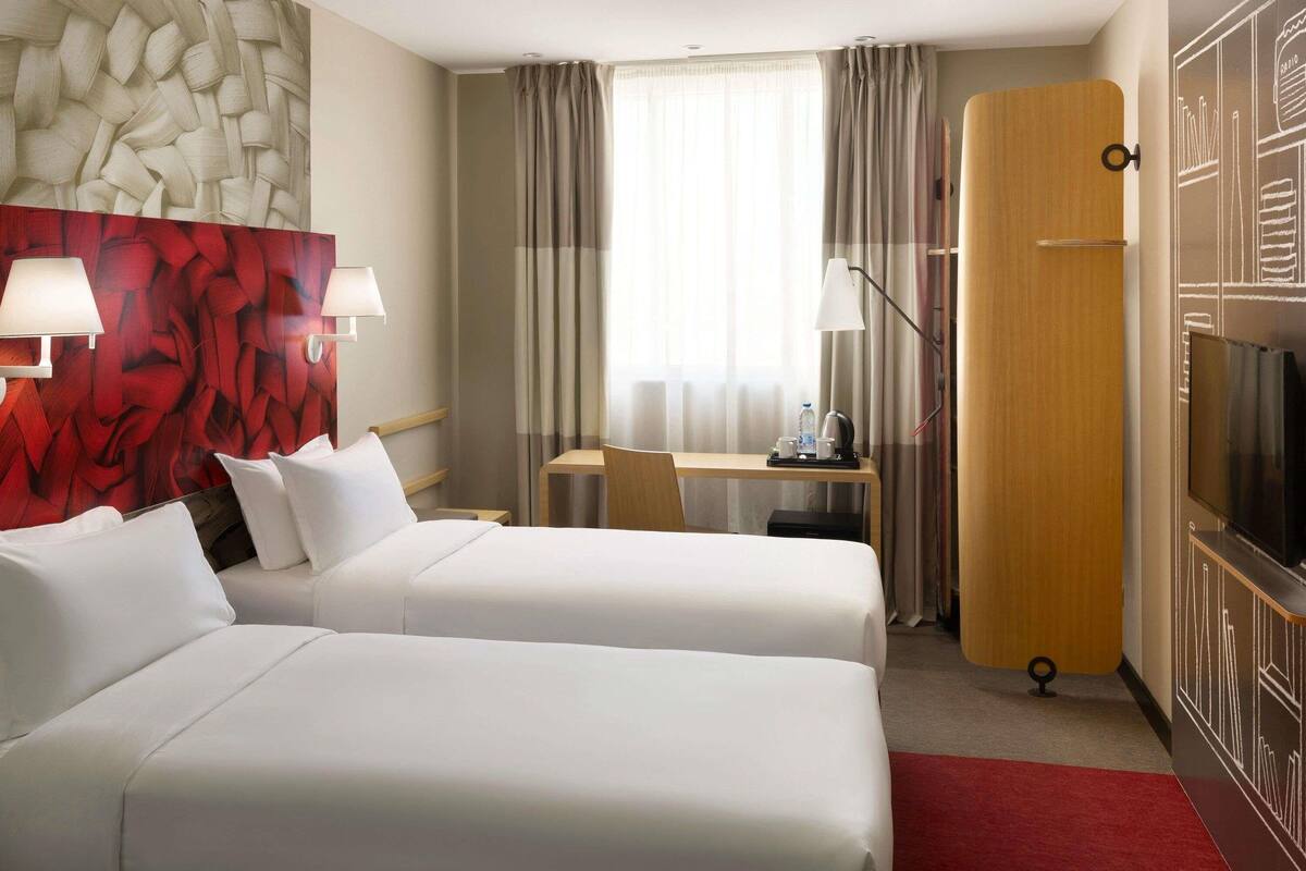 Quarto de hotel com duas camas, uma escrivaninha, televisão e minibar.
