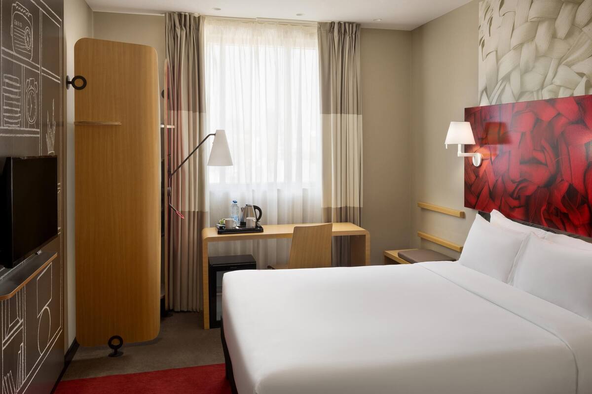 Quarto de hotel com cama, secretária com cadeira, televisão e guarda-roupa.