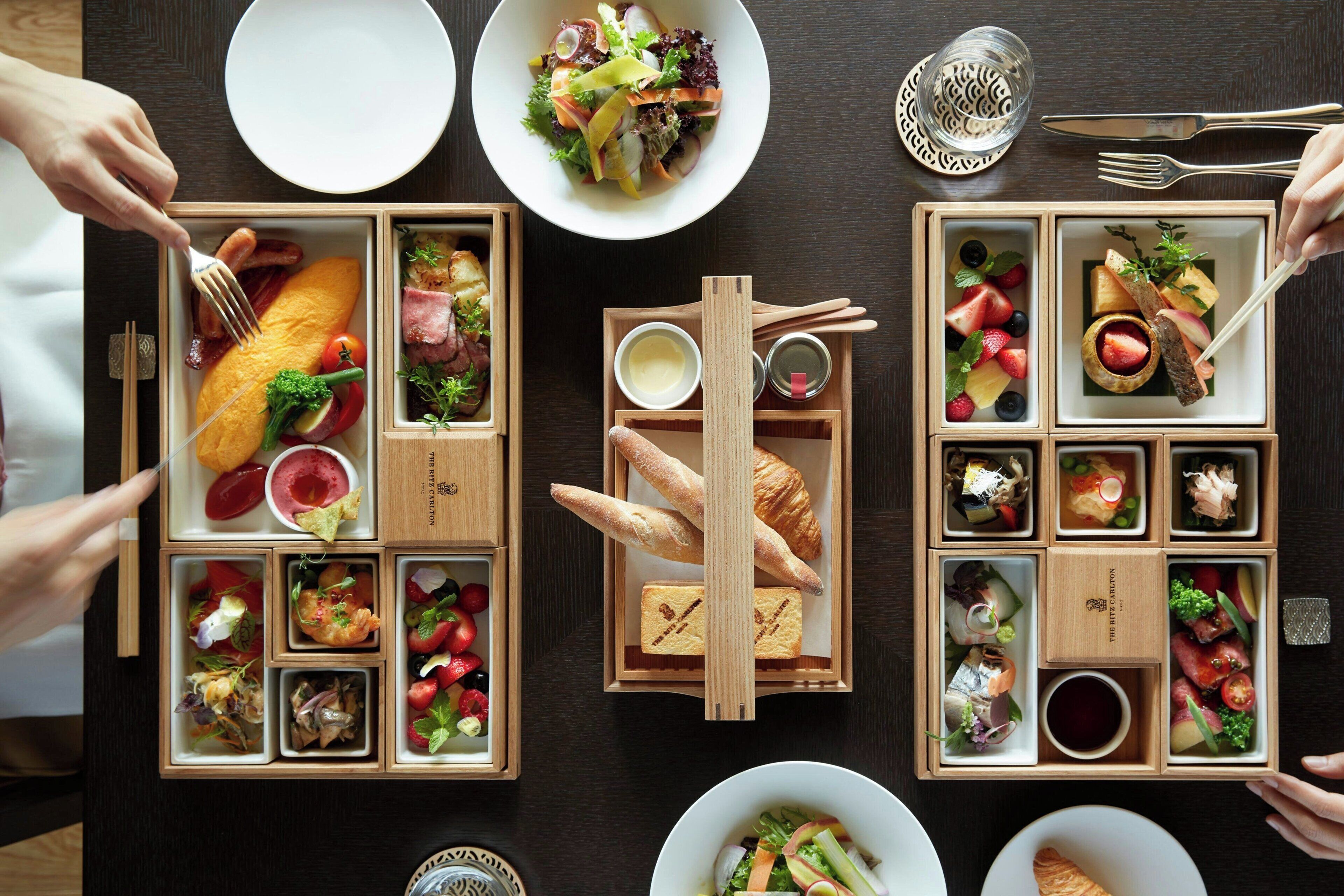 Uma mesa de jantar de madeira com vários compartimentos contendo diferentes alimentos e utensílios.