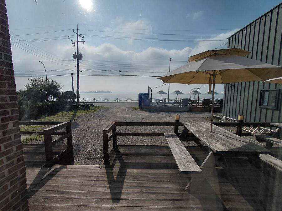 Um deck de madeira que dá para uma área à beira-mar, com bancos e guarda-sóis, com vista para um corpo d'água.