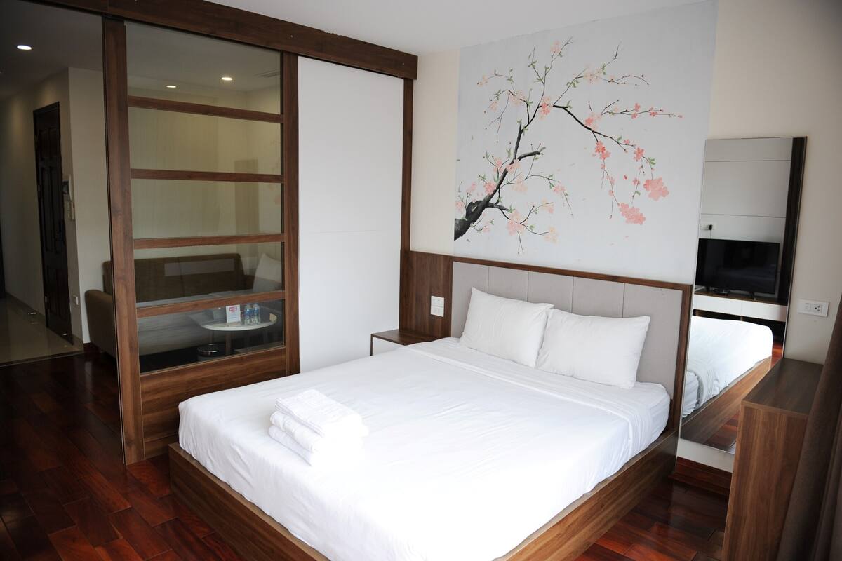 Quarto de hotel moderno com cama de madeira, um espelho grande, televisão na parede e um elemento decorativo na parede.