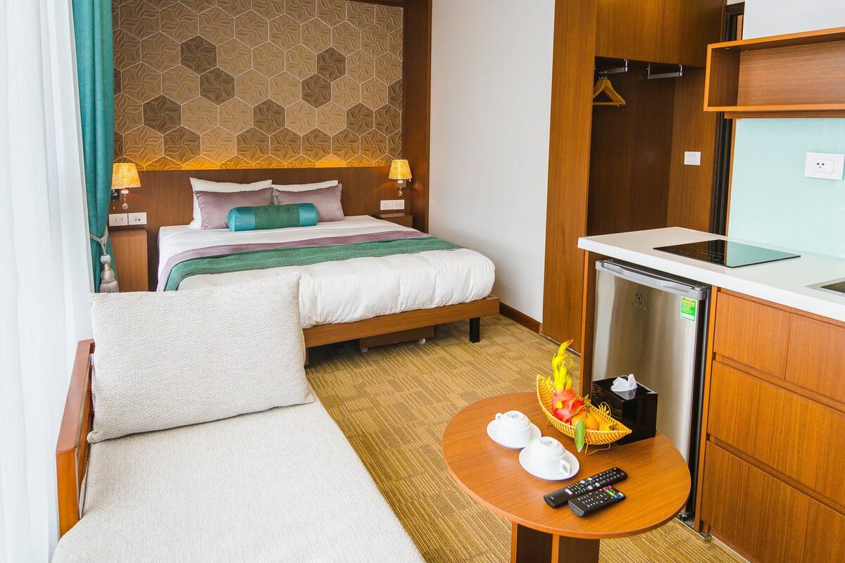 Quarto de hotel com cama, sofá, pequeno espaço de cozinha e banheiro.