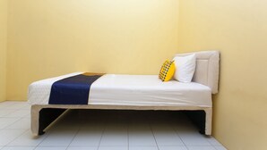 Cama de solteiro com colchão branco, manta azul e dois travesseiros (um branco, um com padrão de bolinhas).