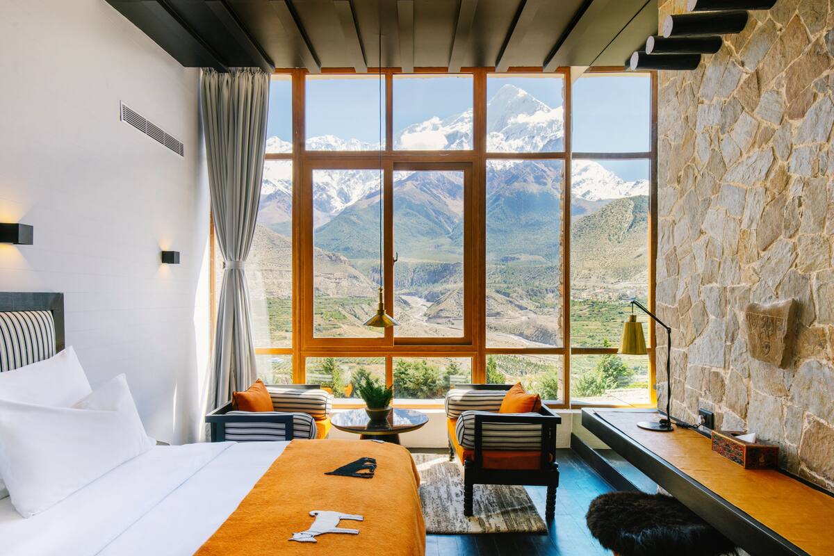 Quarto com uma janela grande, cama, área de estar e parede de pedra.