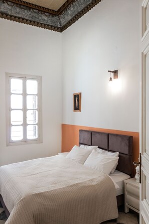 Quarto com cama, mesa de cabeceira, luminária na parede e janela.