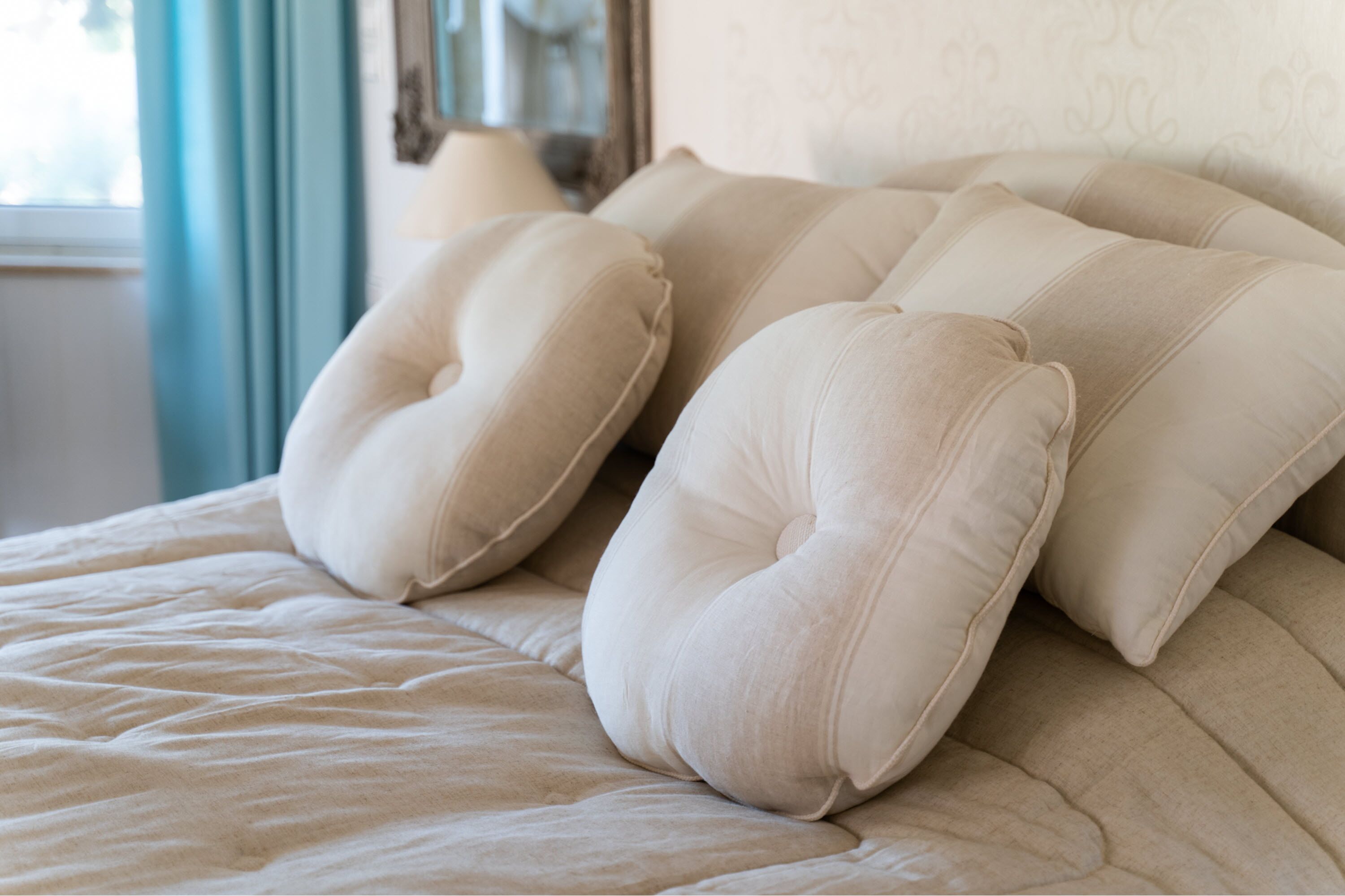 Cama com edredão bege e duas almofadas grandes e com textura.