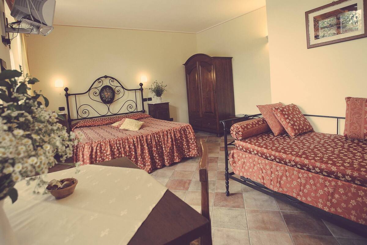 Quarto com duas camas, guarda-roupa de madeira, mesa de cabeceira e um vaso com planta.
