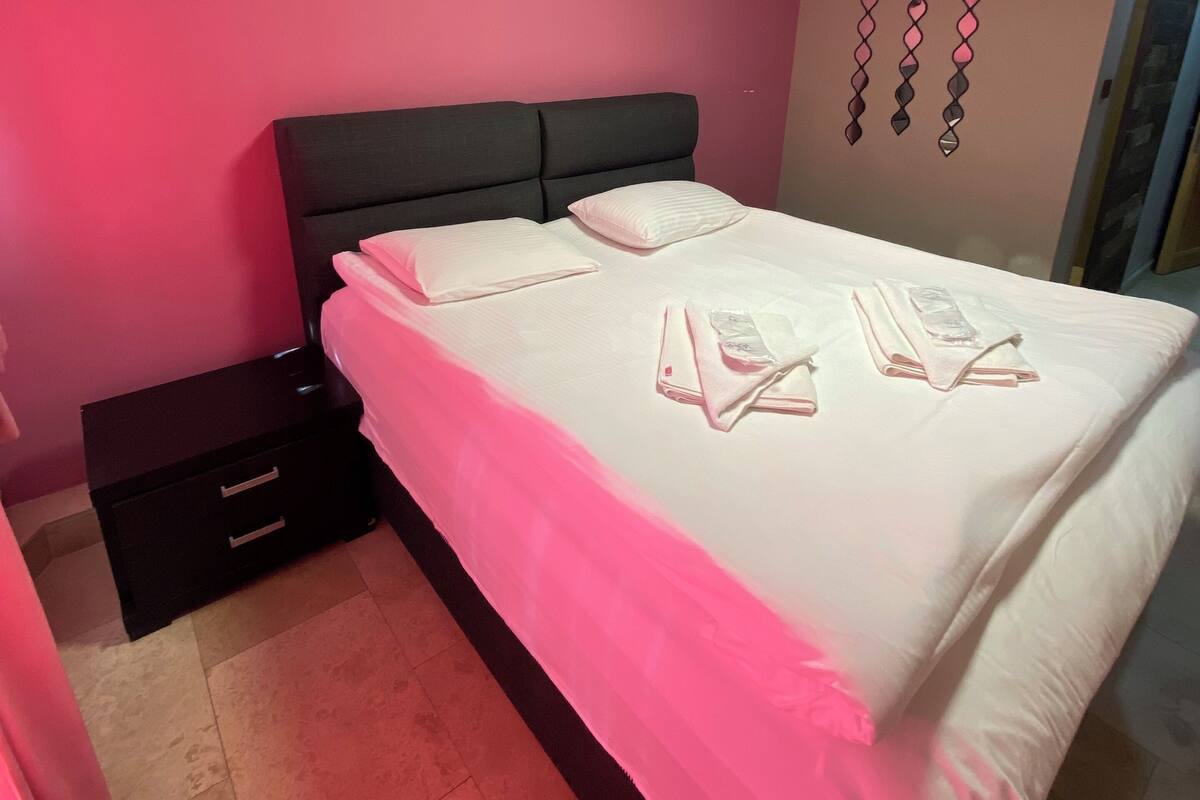 Quarto com cama, mesas de cabeceira e luminária na parede.
