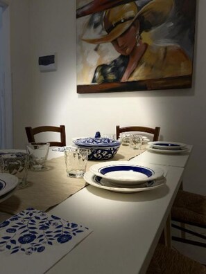 Mesa de jantar posta com pratos, tigelas e copos, com um quadro pendurado acima.