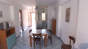 Uma sala de jantar com uma mesa e cadeiras, um ventilador e uma televisão sobre um móvel.