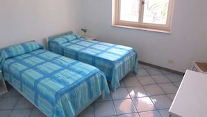 Quarto com duas camas, janela e piso ladrilhado.