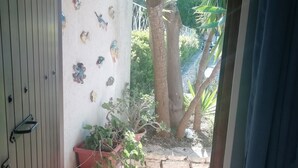 Uma porta arqueada dá acesso a um pátio com parede de pedra, plantas em vasos e uma árvore.