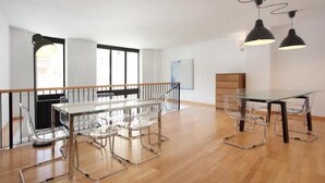 Uma sala de jantar moderna com mesa de vidro, cadeiras de metal, corrimão de madeira e luminárias pendentes pretas.