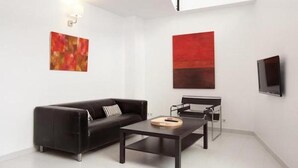 Uma sala de estar moderna com um sofá de couro preto, uma mesa de centro e duas pinturas abstratas nas paredes.