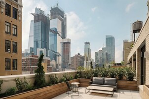 Terraço no telhado com vista para a cidade, mobiliário ao ar livre e vasos de plantas.