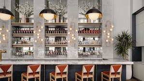 Uma área de bar com várias prateleiras de garrafas, banquetas e iluminação pendente.