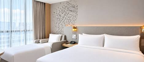 Quarto de hotel com duas camas, uma janela grande com cortinas, luminária na parede e telefone na mesa de cabeceira.