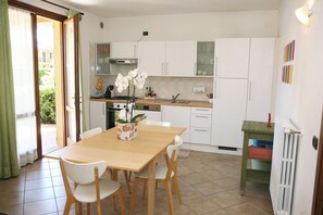 Uma cozinha moderna com armários brancos, uma mesa de jantar de madeira e cadeiras. Há um fogão, uma pia e uma pequena planta sobre a mesa.