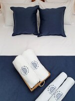 Cama bem arrumada com dois travesseiros azuis marinhos e um conjunto de toalhas brancas com um logotipo.