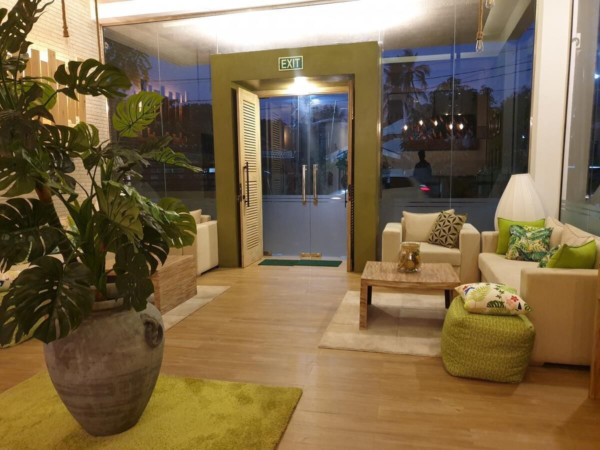 Um hall de hotel com um balcão de recepção, uma grande planta em vaso, um conjunto de sofás e uma porta de saída.