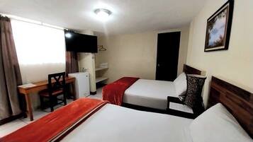 Quarto de hotel com duas camas, uma escrivaninha, uma cadeira, uma televisão e uma porta.