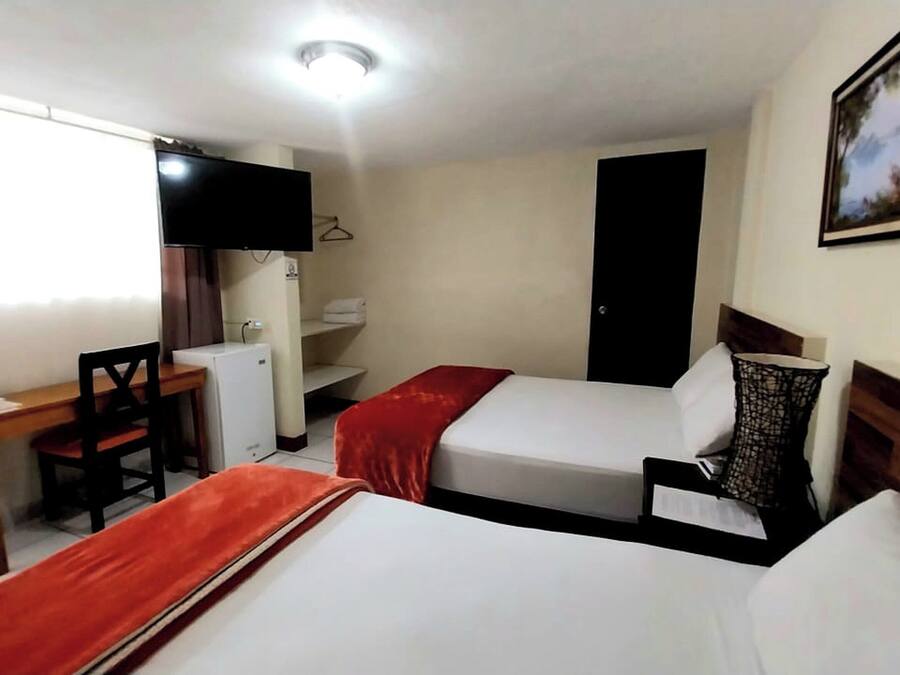 Quarto de hotel com duas camas, uma escrivaninha, uma cadeira, uma televisão e uma porta.