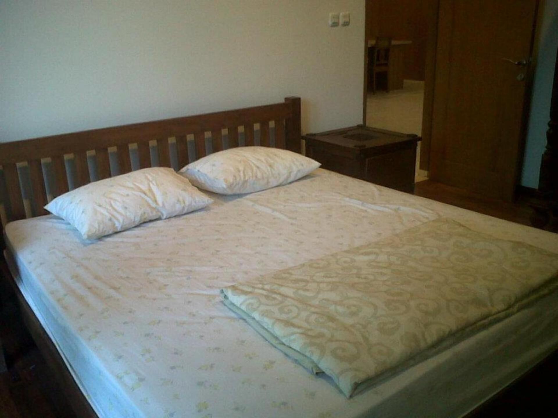 Cama com cabeceira de madeira, duas almofadas e colcha estampada.