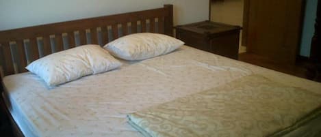 Cama com cabeceira de madeira, duas almofadas e colcha estampada.