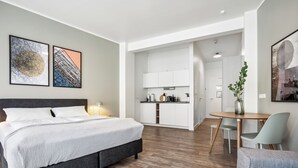 Quarto de hotel moderno com cama, escrivaninha e cozinha compacta.