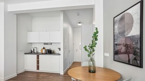 Uma cozinha moderna com armários brancos, uma mesa de jantar de madeira e um vaso com folhas verdes.