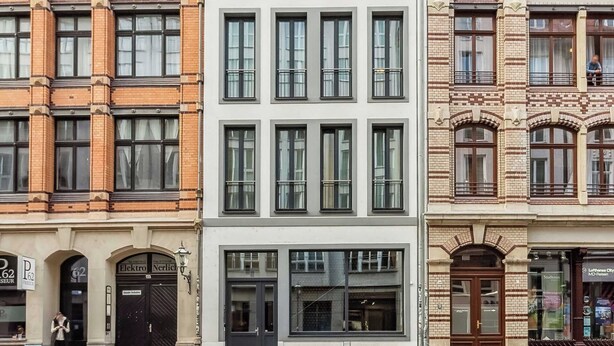 Uma fileira de edifícios com três andares e estilos arquitetônicos distintos, incluindo fachadas de tijolo e grandes janelas.