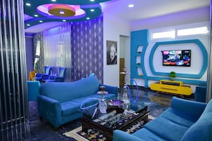 Uma sala de estar moderna com sofás azuis, uma mesa de centro de vidro, uma TV e um cachimbo decorativo.