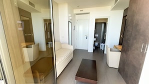 Uma sala de estar moderna com um painel de vidro, um sofá, uma mesa de centro e uma porta que dá para um banheiro.