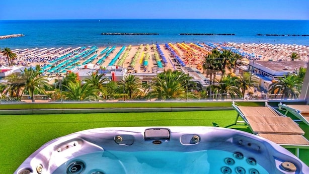 Um resort à beira-mar com fileiras de espreguiçadeiras e guarda-sóis, uma piscina e vista para o oceano.