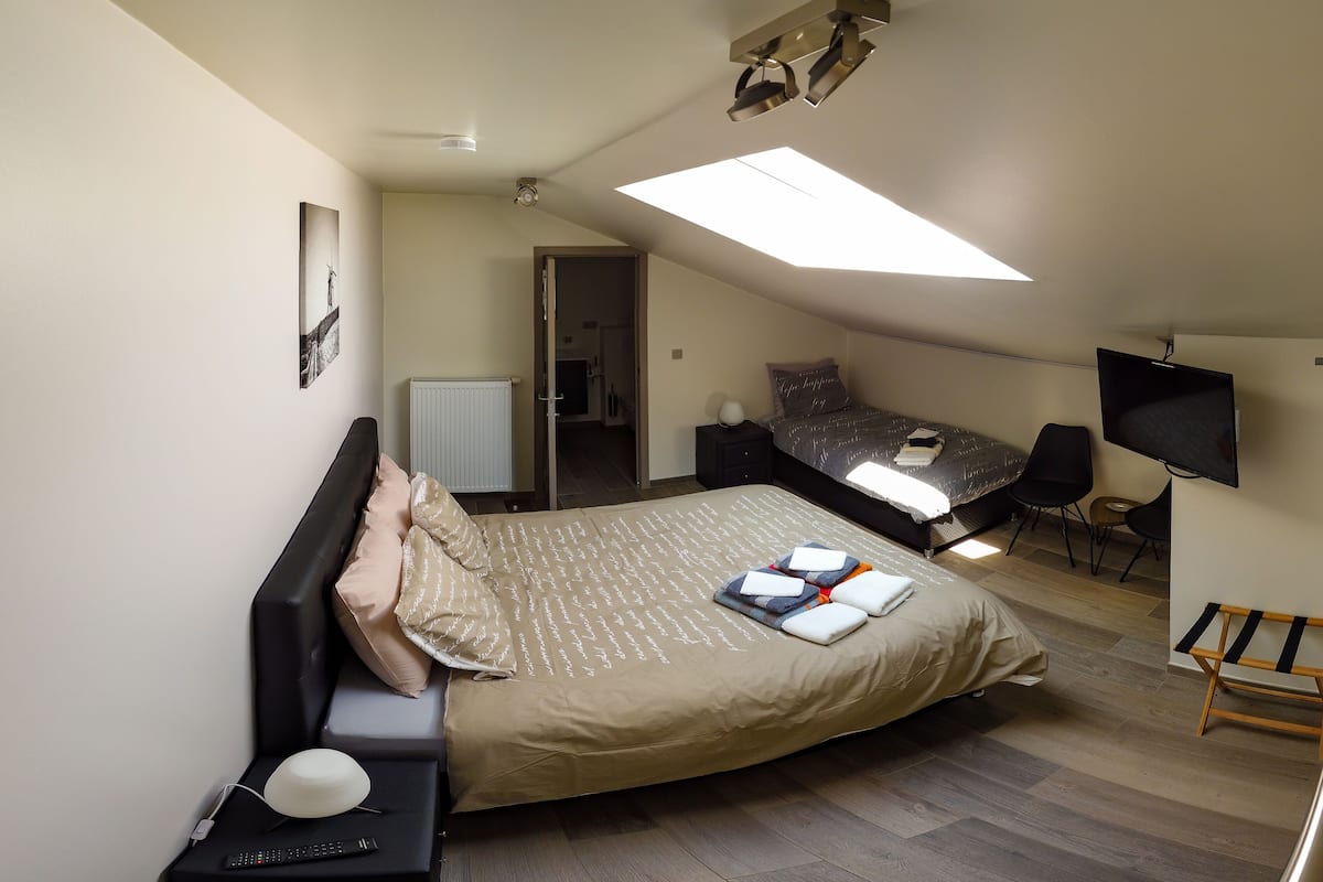 Quarto com cama grande, escrivaninha, cadeira, televisão e claraboia.