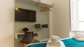Quarto de hotel com cama, escrivaninha, cadeira, televisão e janela.