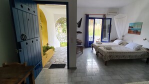 Quarto com duas camas, uma mesa de jantar e vista para o jardim através de uma porta aberta.
