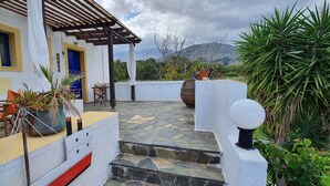 Um pátio com piso de pedra, plantas em vasos, pérgola de madeira e vista para uma montanha.