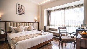 Quarto de hotel com uma cama grande, uma escrivaninha, uma cadeira e uma janela com cortinas.