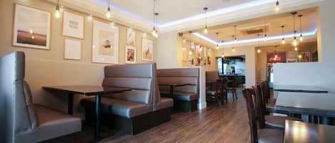 Um restaurante moderno com assentos em cabines e mesas, piso de madeira e luminárias pendentes.