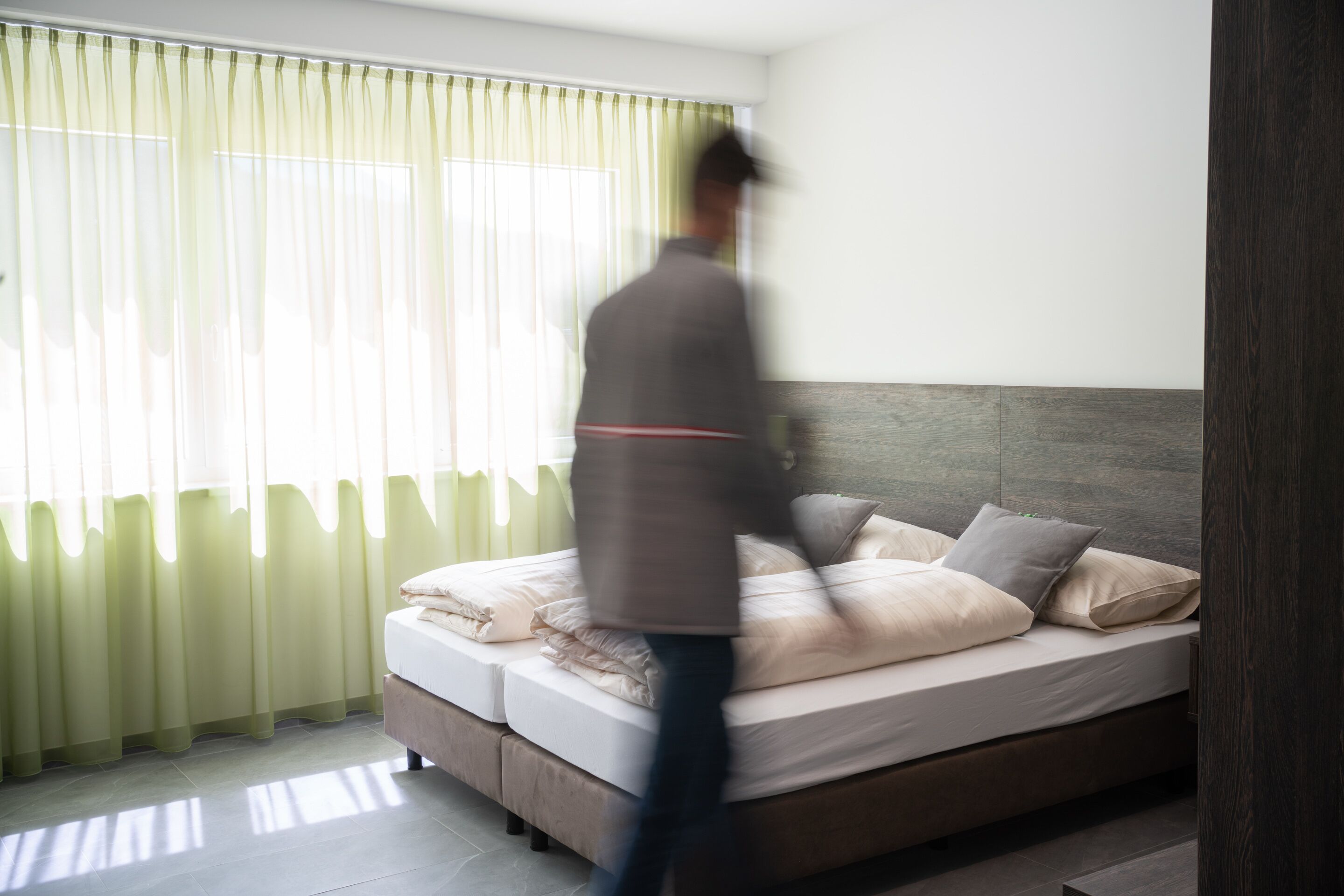 Um quarto moderno com uma cama grande, cabeceira de madeira e cortinas translúcidas.